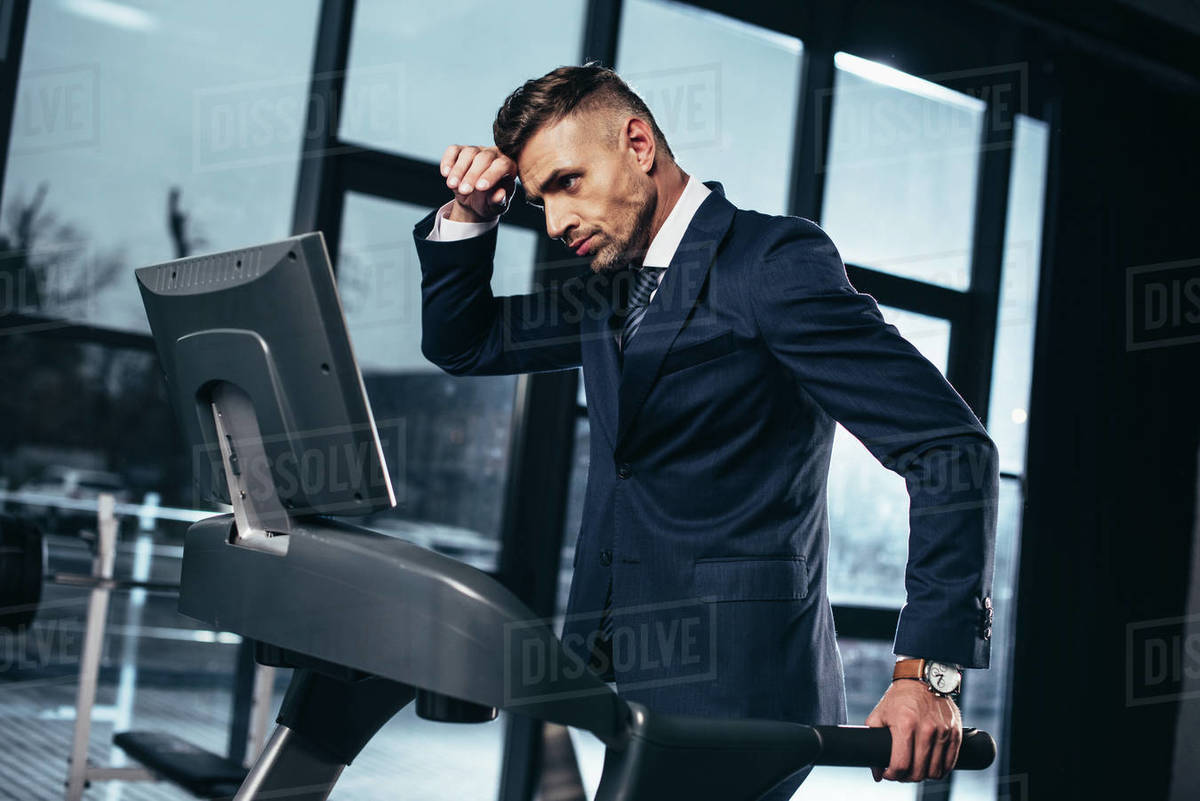 Side view of tired handsome businessman in suit exercising on treadmill ...