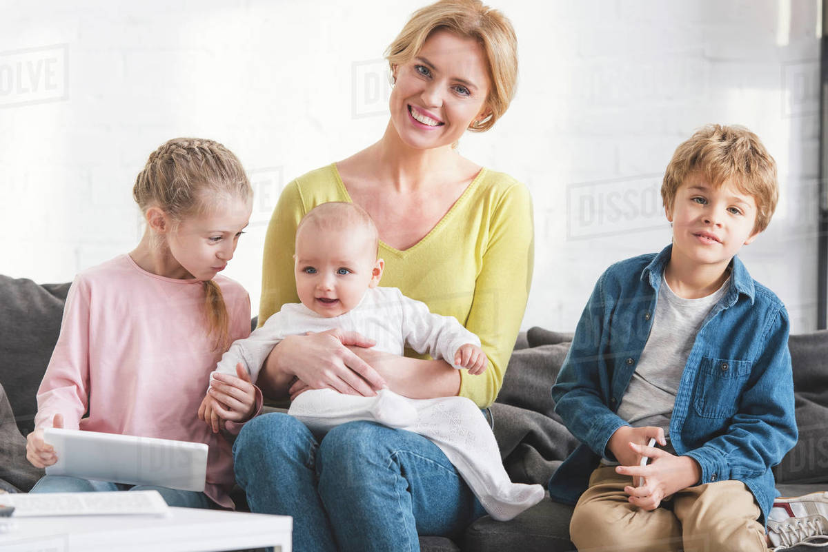 Beautiful happy mother smiling at camera while sitting on couch with ...