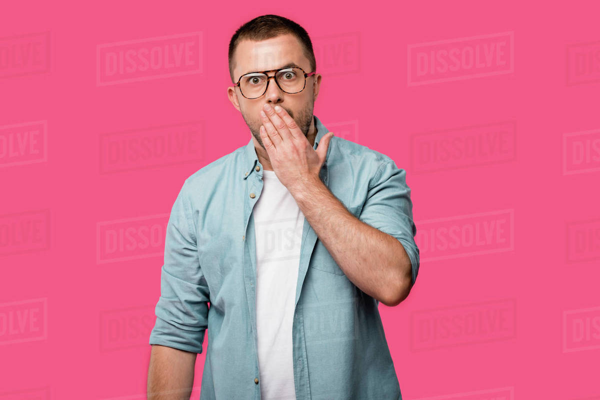 shocked young man holding hand over mouth and looking at camera ...