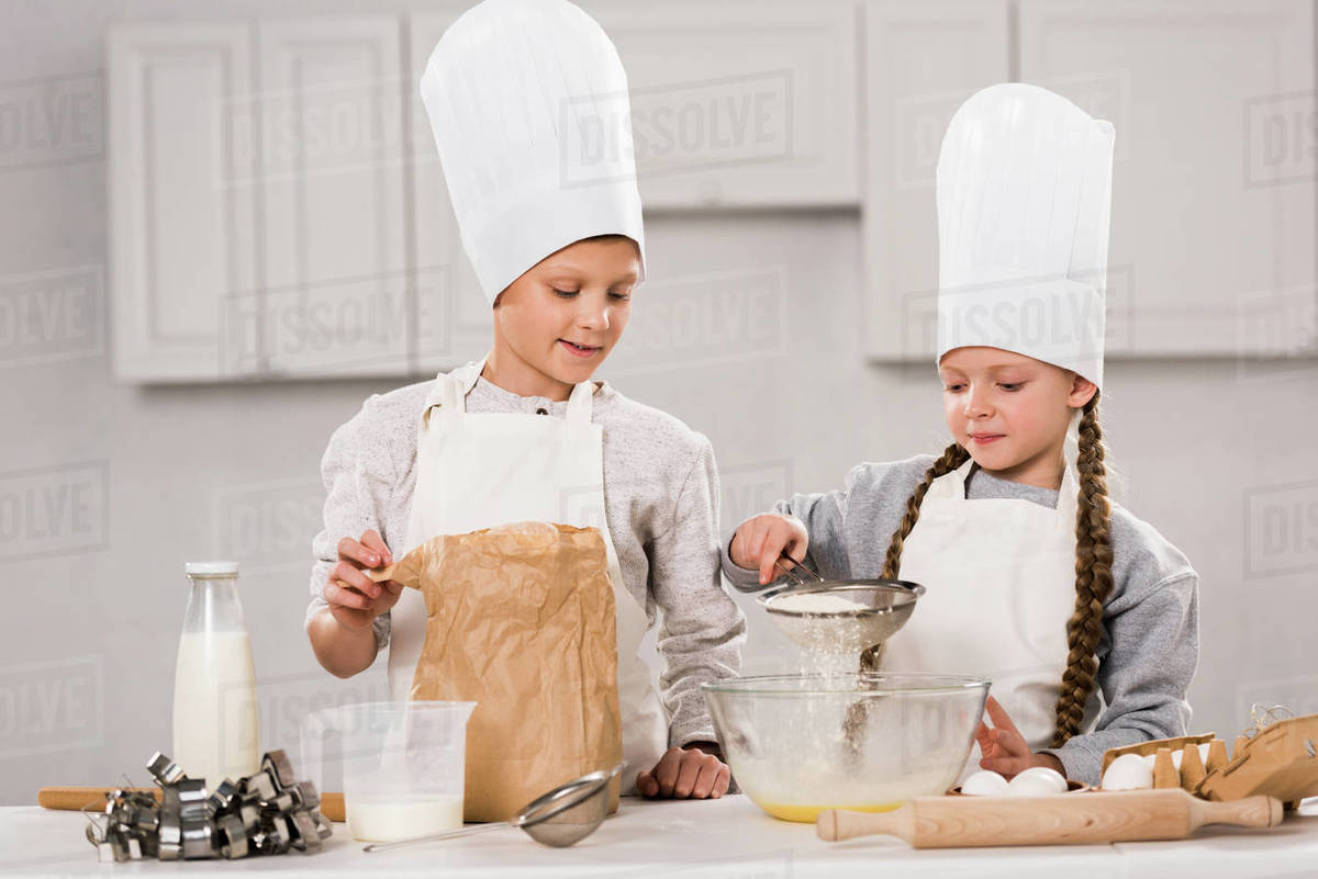 happy kids in aprons sifting flour through sieve into bowl at table in ...
