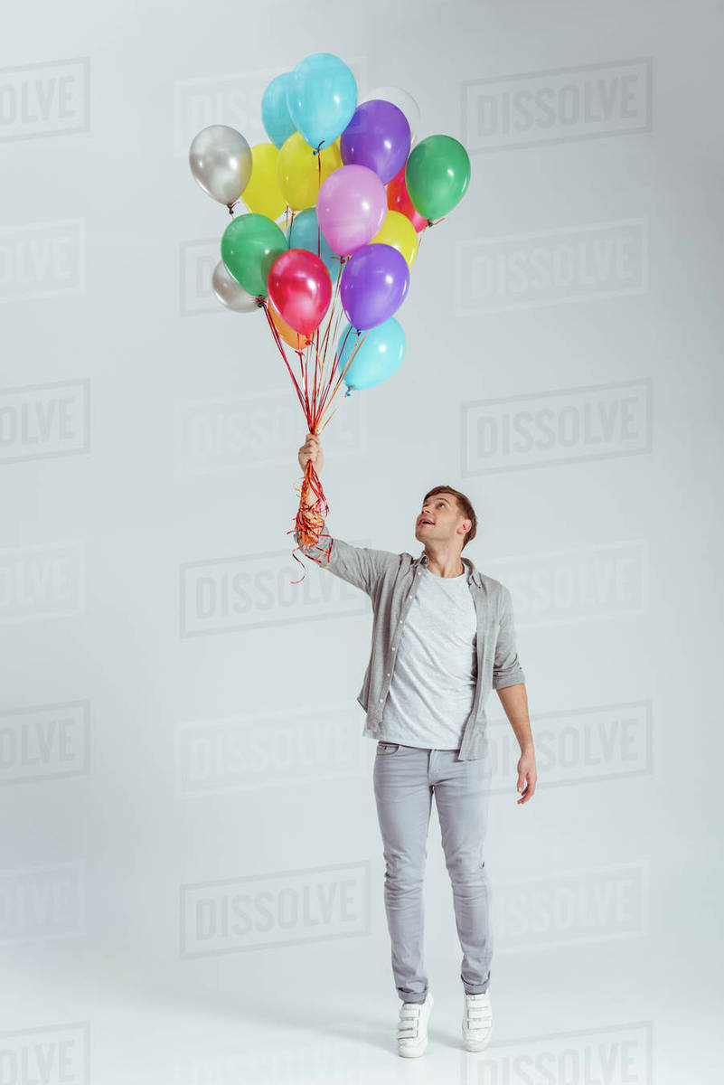 handsome man standing on tiptoe and holding bundle of colorful balloons ...