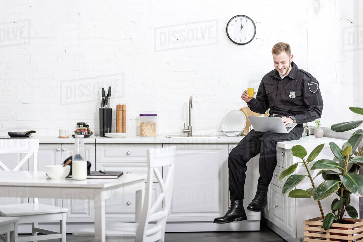 Young policeman sitting on table, drinking orange juice and using ...