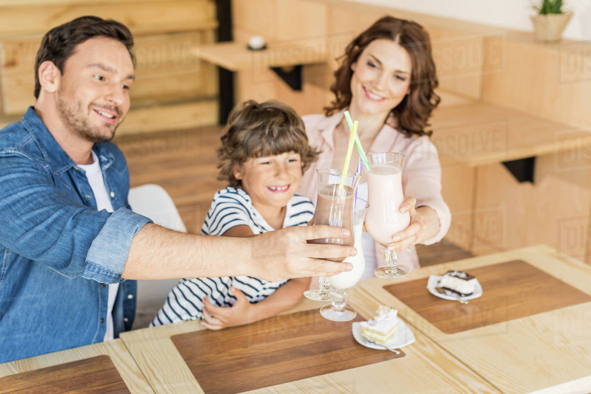 Happy young family drinking milkshakes in cafe and spending time ...