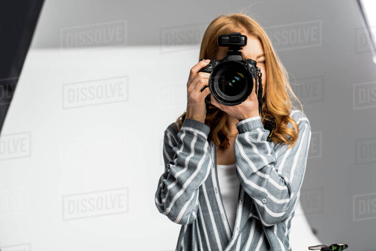 Beautiful young female photographer shooting with professional camera ...
