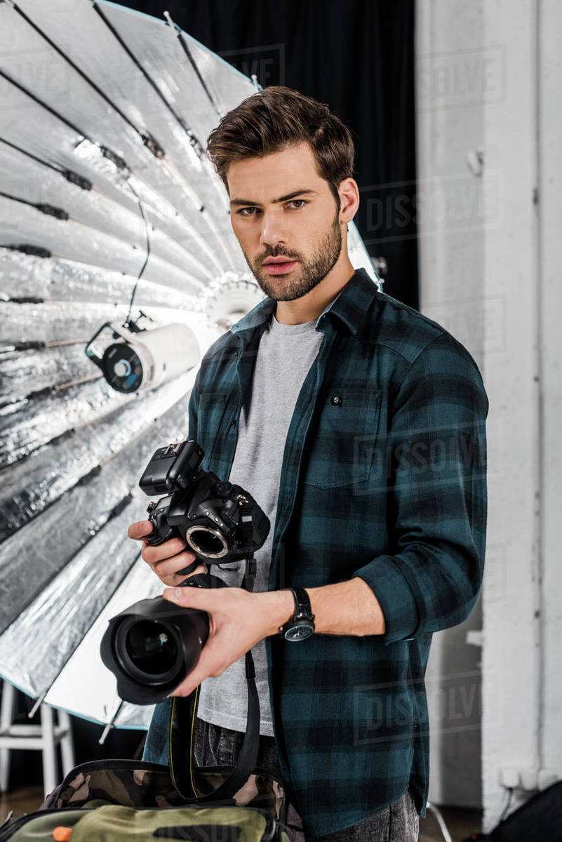 Handsome professional young photographer holding camera and lens in ...