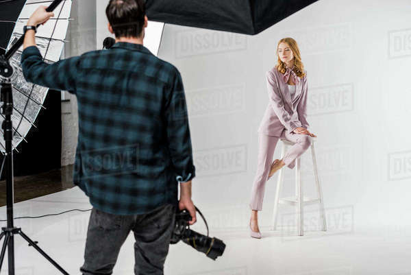 Back view of photographer holding camera and model posing in studio ...