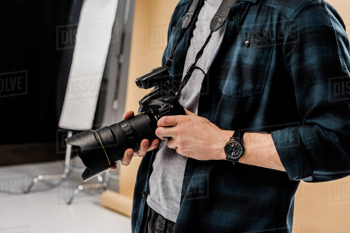 Cropped shot of young photographer holding camera in photo studio ...