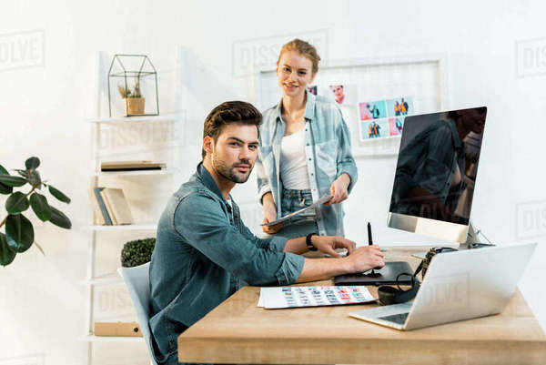 Young photographers smiling at camera while retouching photos in office ...