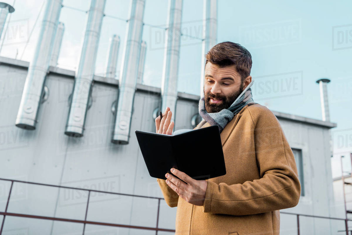 Confused businessman looking at notebook in beige coat - Royalty-free ...
