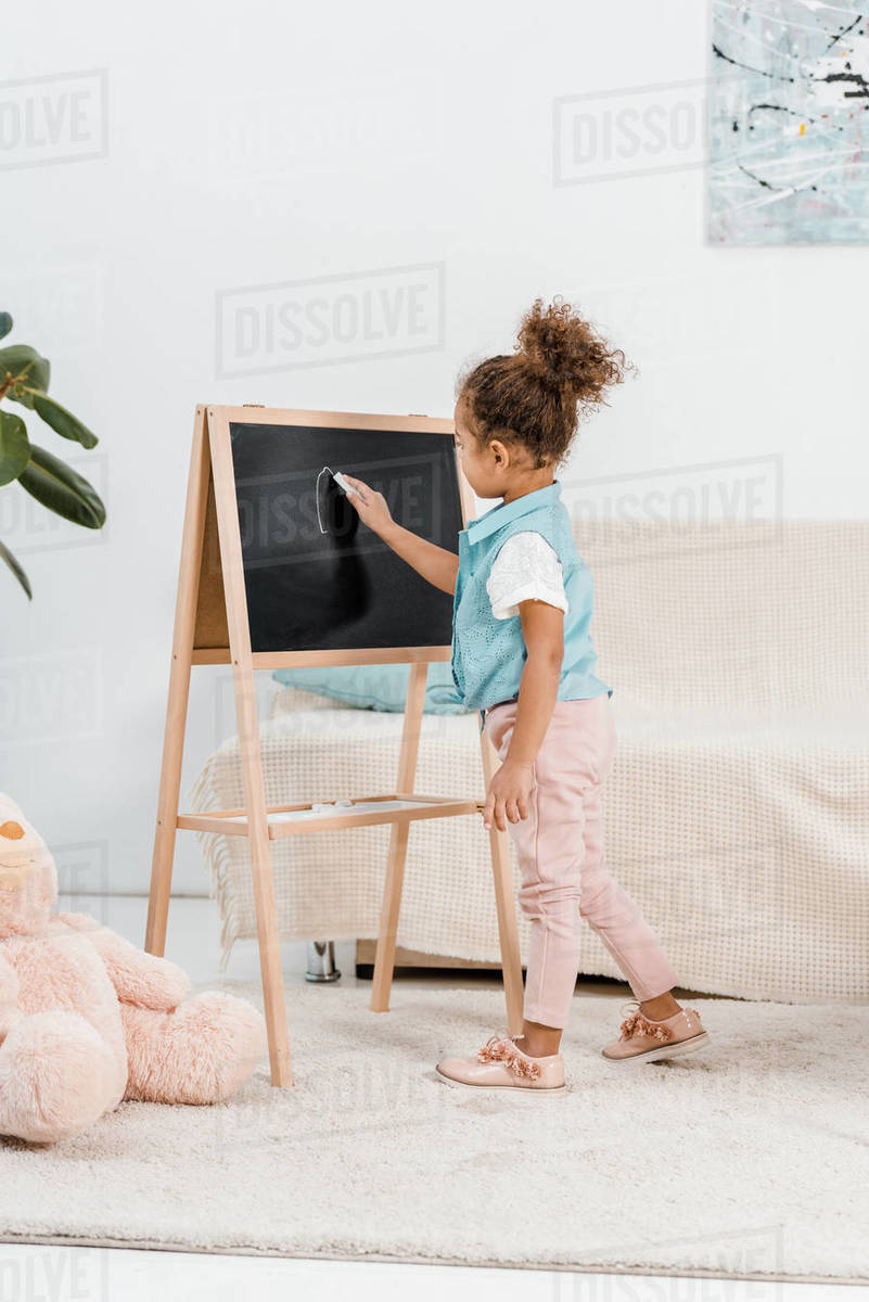 Adorable African American child standing and writing on chalkboard ...