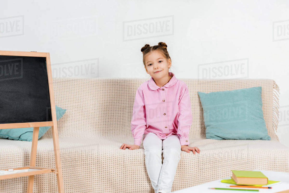 Full length view of beautiful little child sitting on couch and smiling ...