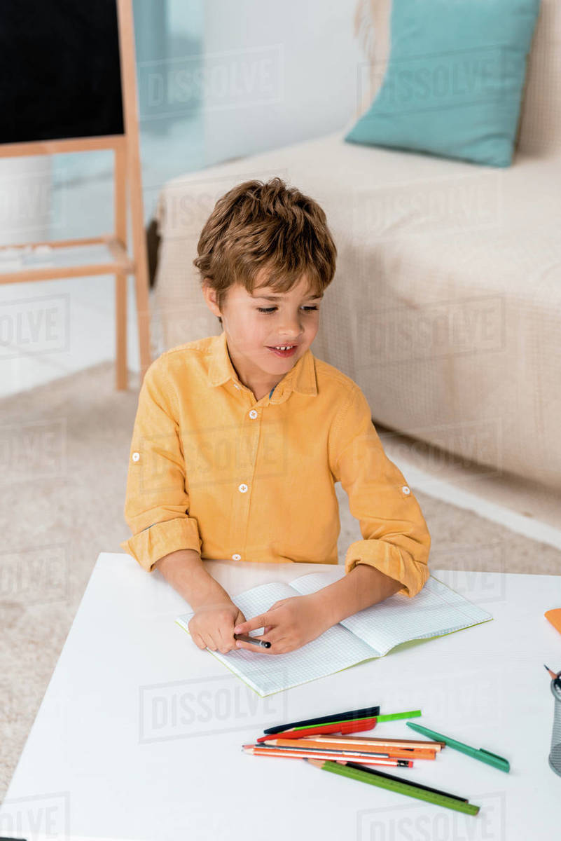 High angle view of cute little boy sitting at table and studying at ...