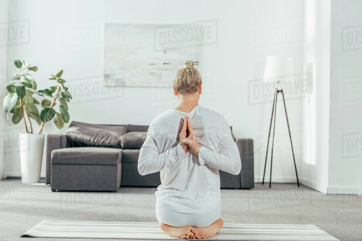Back view of man sitting in yoga pose with hands behind back at home ...