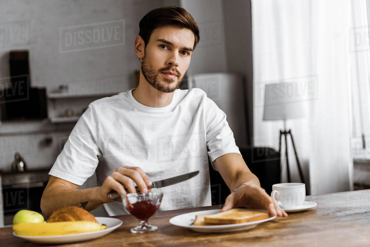 handsome young man having toasts with jam and fruits for breakfast and ...