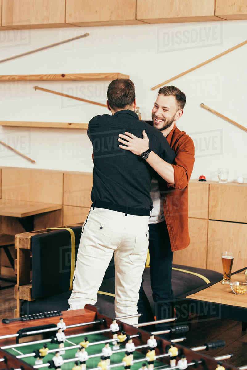 cheerful men hugging while greeting each other in cafe - Royalty-free ...