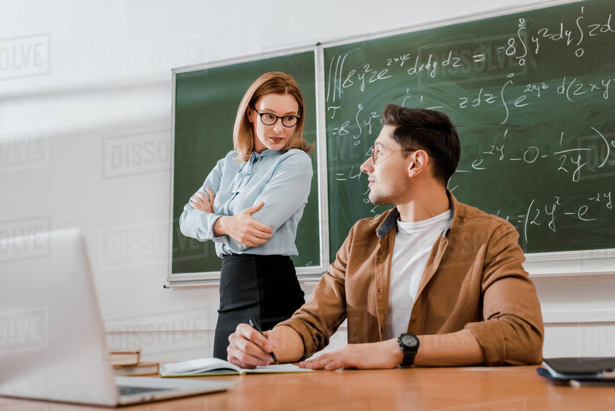 Female professor standing with crossed arms and looking at student in ...