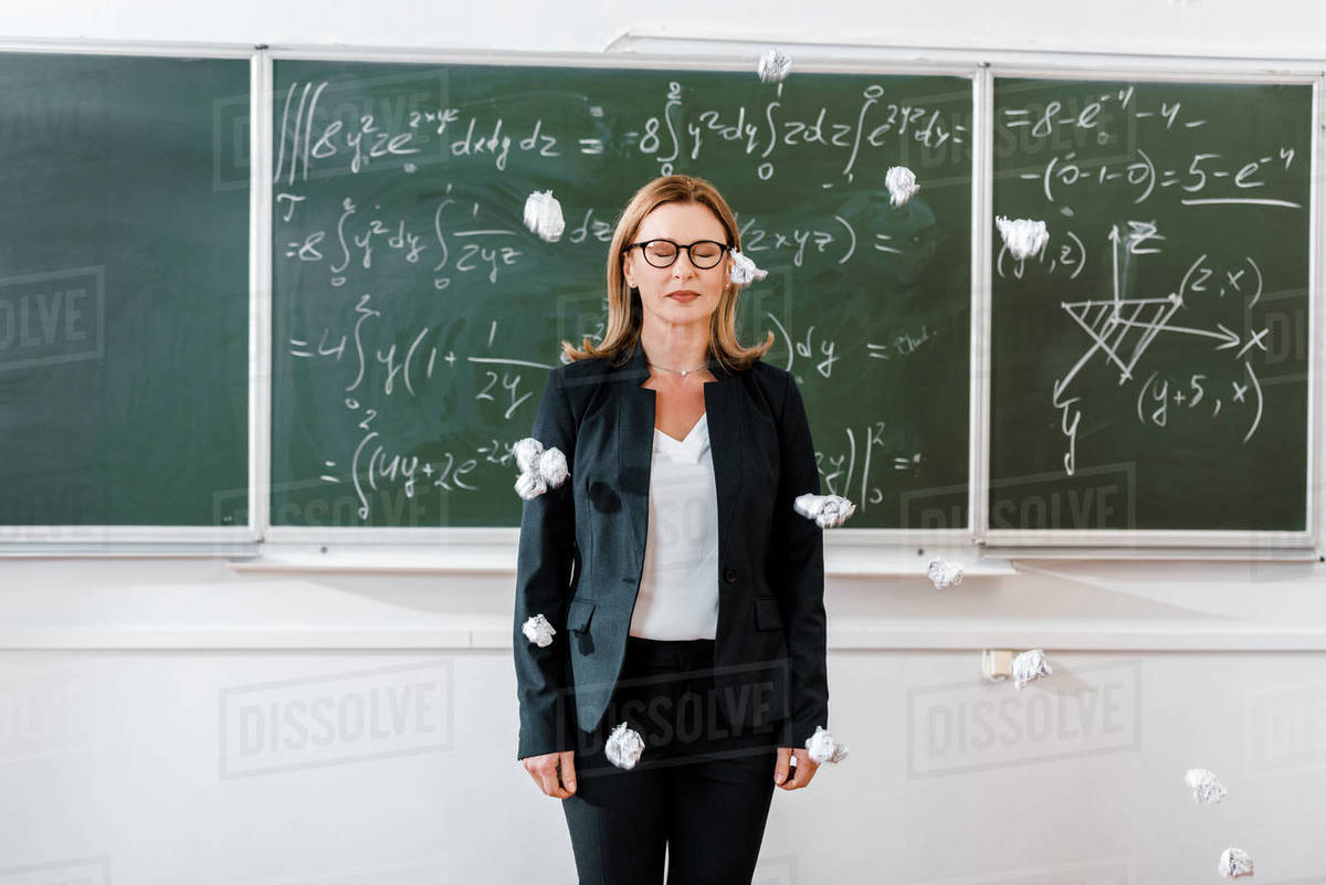 Crumpled paper balls flying at female teacher in classroom with ...