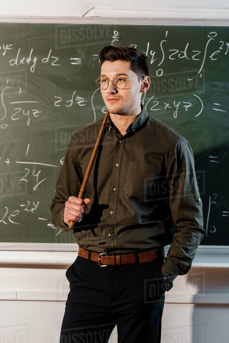 Serious male teacher in formal wear holding wooden pointer in front of ...