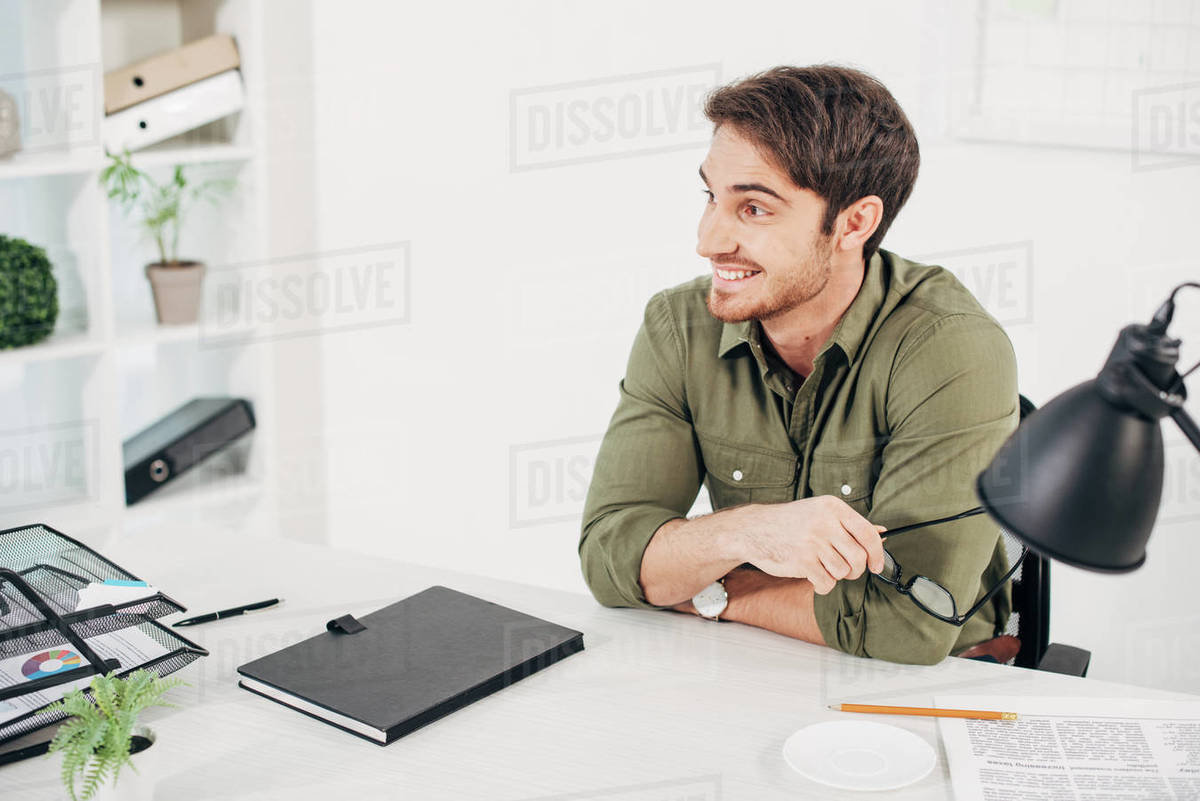 Handsome office manager sitting at desk with notebook and papers ...