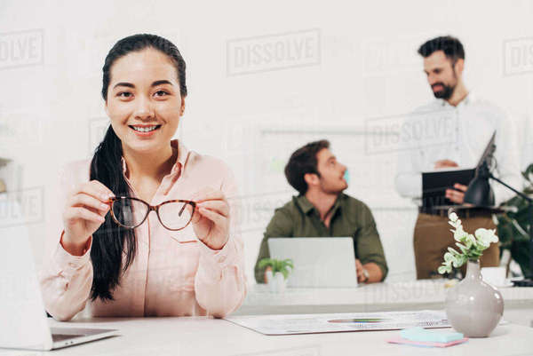 Young female manager holding glasses and smiling in office - Royalty ...