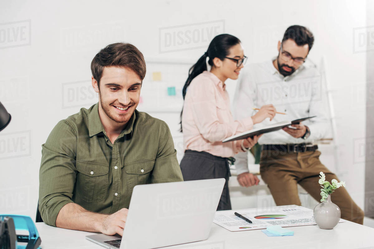 Male office manager using laptop with colleagues on background - Stock ...