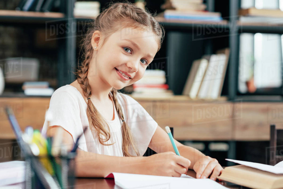 Happy smiling little girl writing homework - Stock Photo - Dissolve