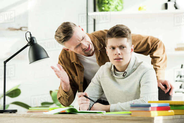 Angry father gesturing and screaming at teen son, boy covering ears ...