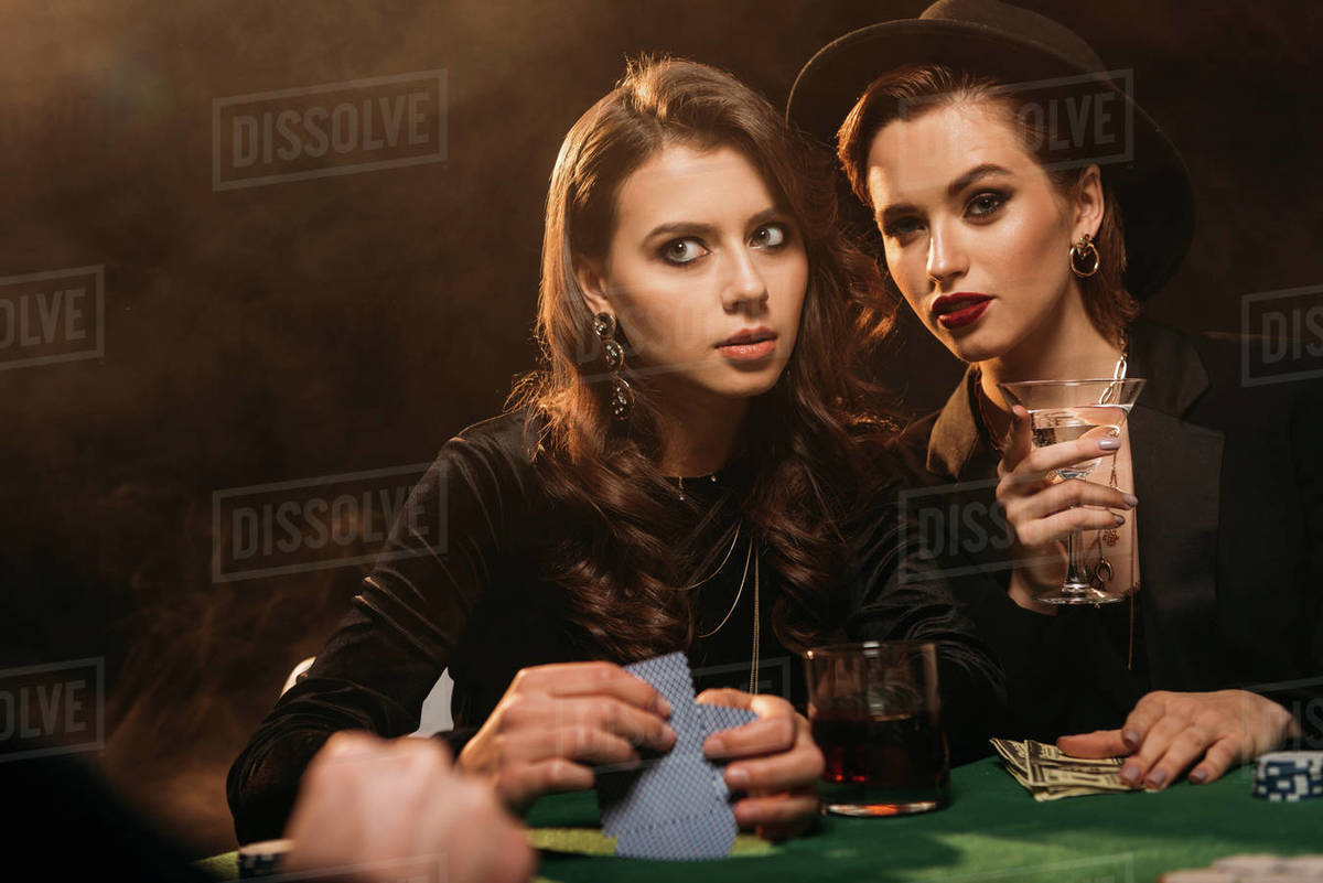 Beautiful women playing poker at table in casino and looking away ...