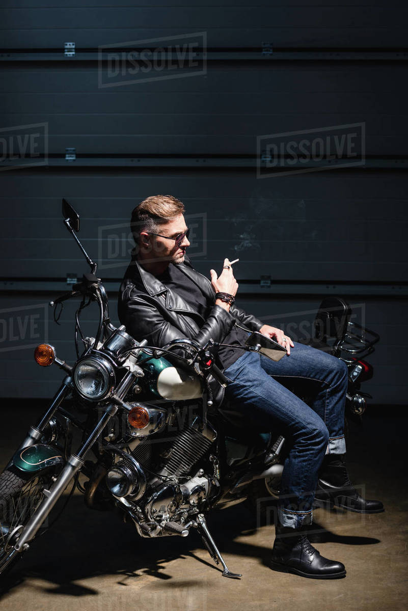 Handsome guy in sunglasses leaning on motorcycle in garage - Royalty ...