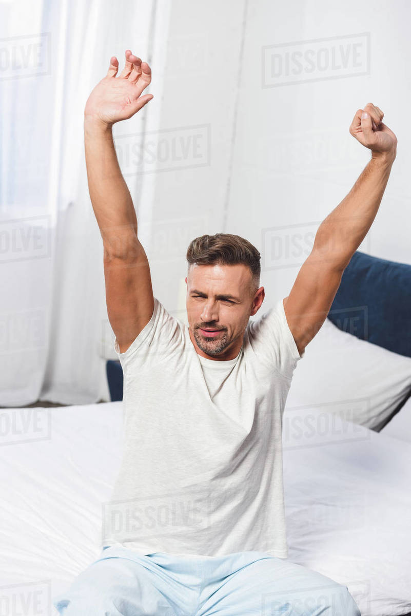 Sleepy man sitting on bed and yawning - Royalty-free Stock Photo | Dissolve