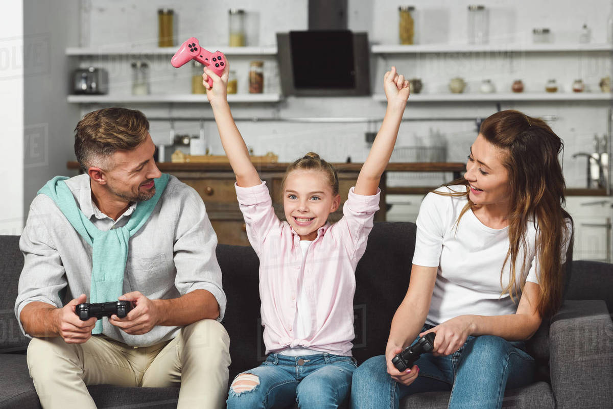 Happy daughter rejoicing victory while playing video game with parents ...