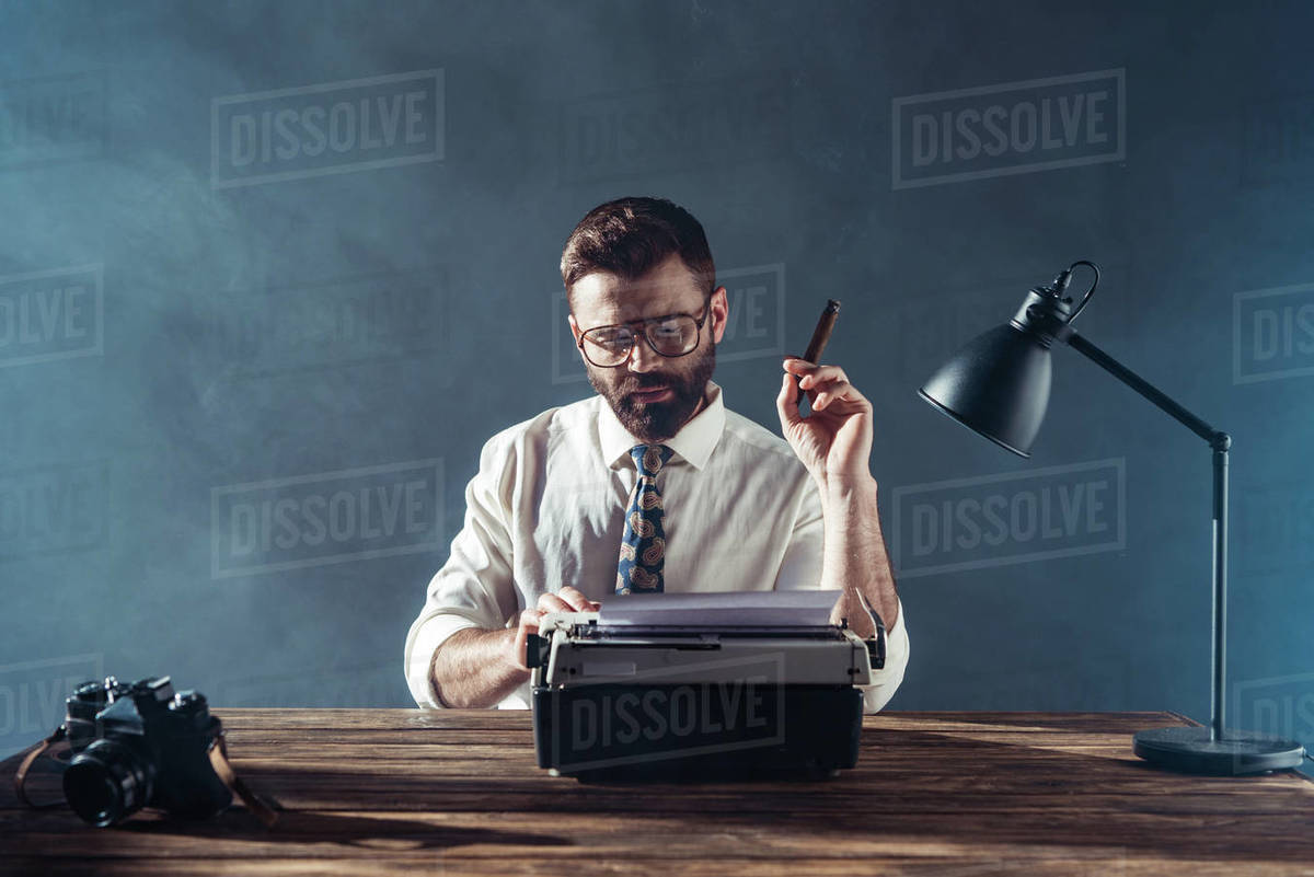 Handsome journalist in glasses sitting at table with retro typewriter ...