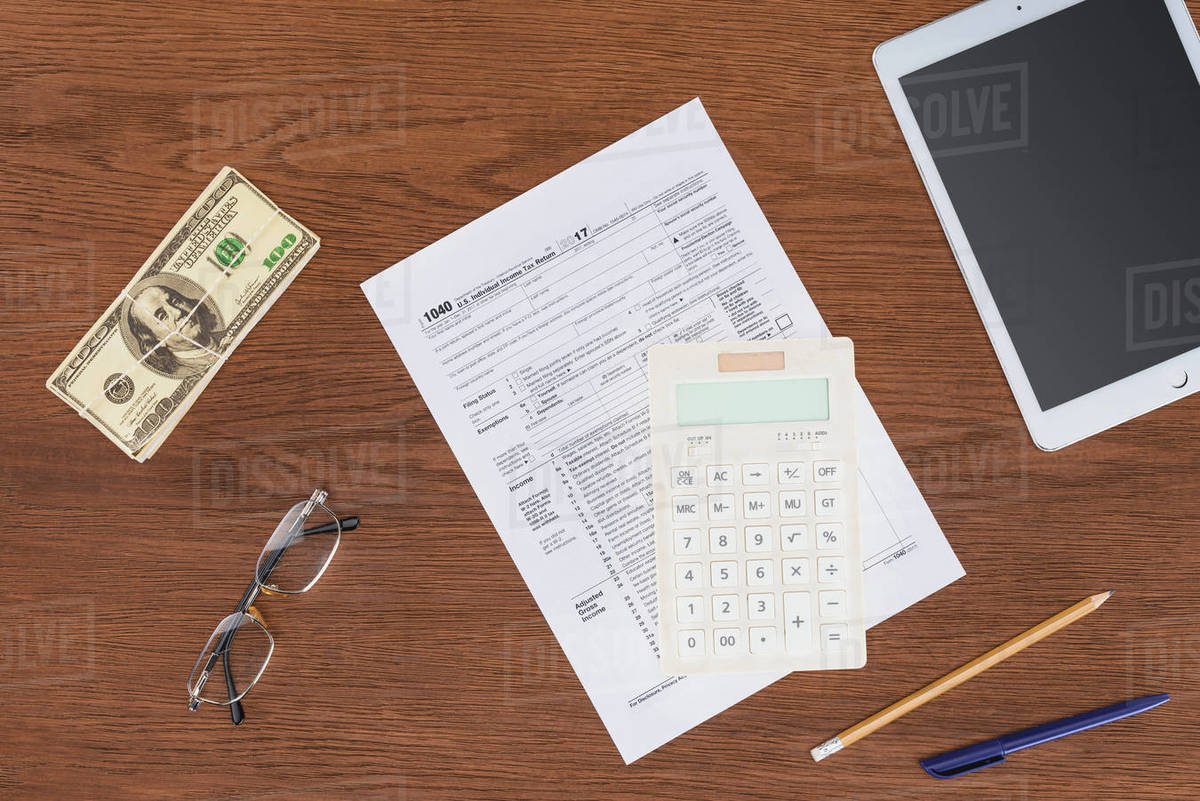 Top view of tax form, calculator and dollar banknote on wooden desk at ...
