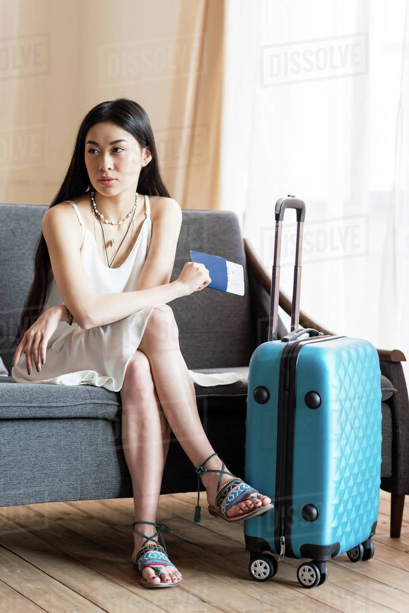 Asian woman traveler sitting on sofa with suitcase and passport ...