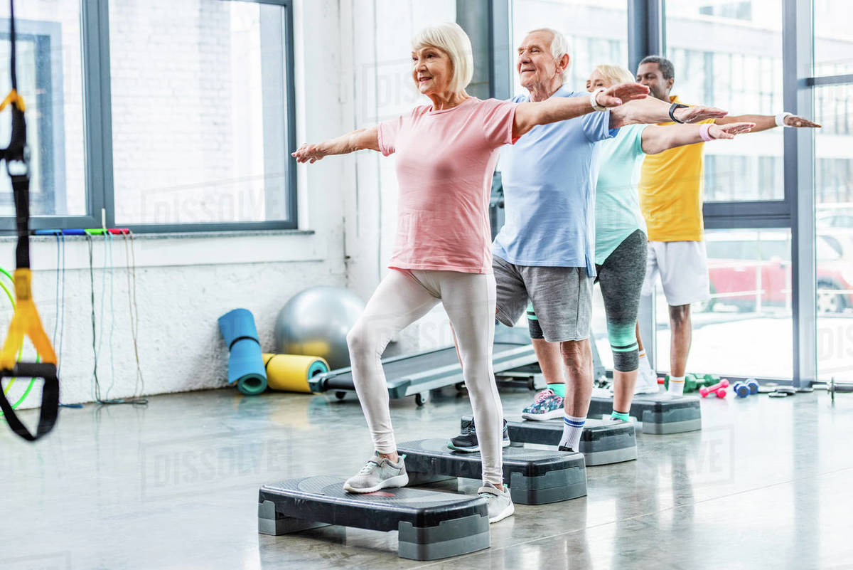 Multicultural senior athletes synchronous exercising on step platforms ...