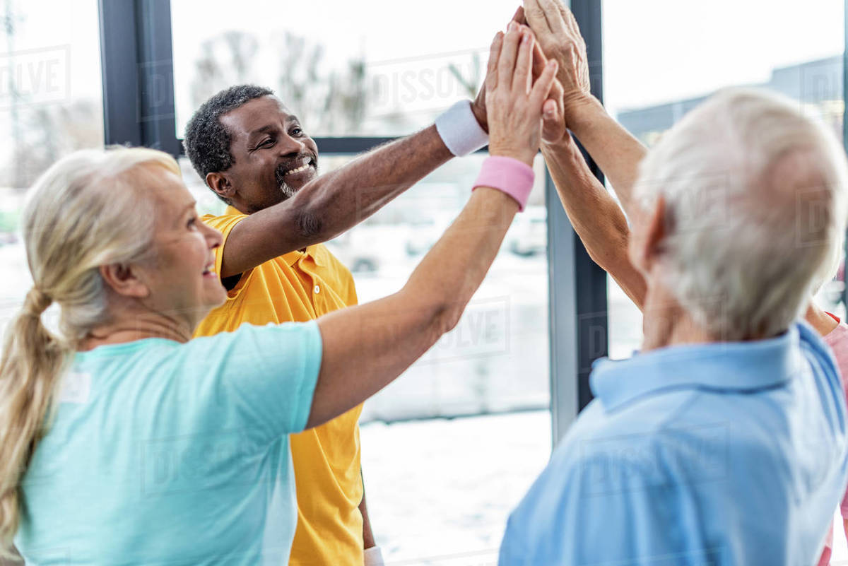 Happy senior multicultural sportspeople putting hands together at gym ...