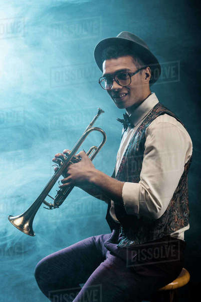 Happy young jazzman posing with trumpet on stage with dramatic lighting ...