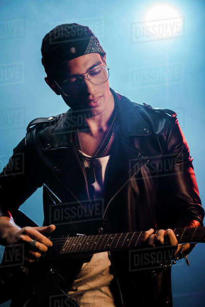 Focused male rock star in leather jacket performing on electric guitar ...