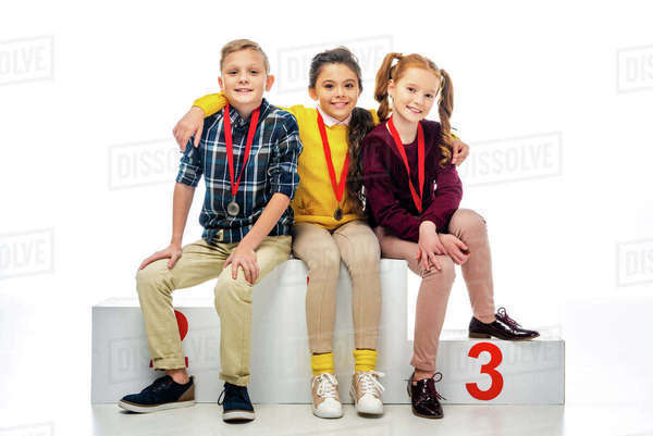 Smiling kids with medals sitting on winner podium and looking at camera ...