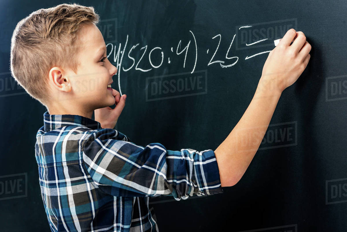 Smiling boy writing math example on blackboard with chalk - Royalty ...
