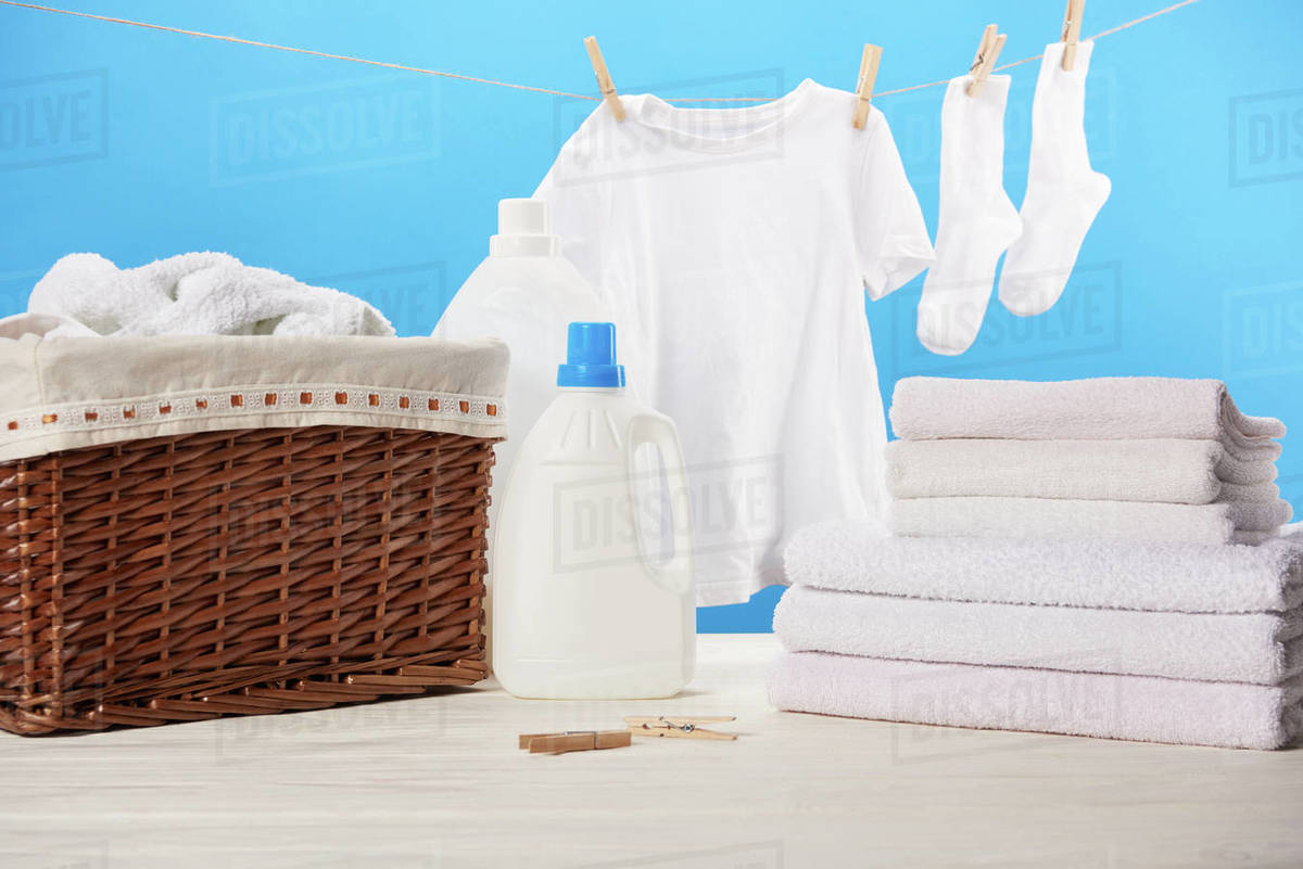 Plastic containers with laundry liquids, laundry basket, pile of towels ...