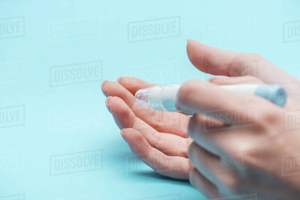 Cropped view of female hands testing glucose level with needle on blue ...