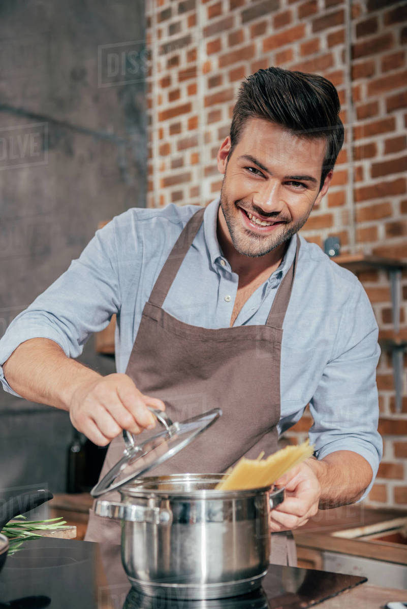 Handsome young man with apron cooking pasta - Royalty-free Stock Photo ...