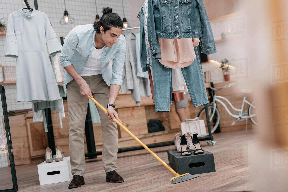 Handsome young man with broom sweeping floor in shop before opening ...