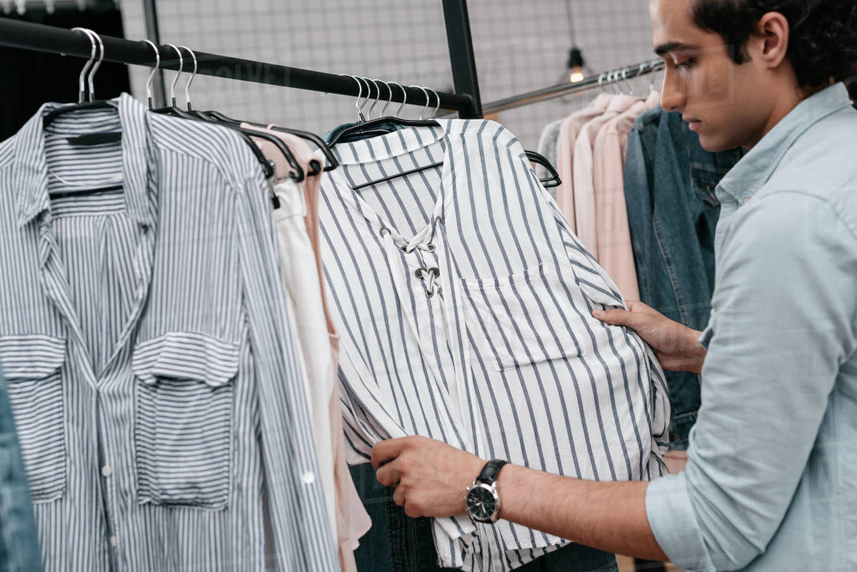 Focused young man working with clothes on hangers in store - Royalty ...