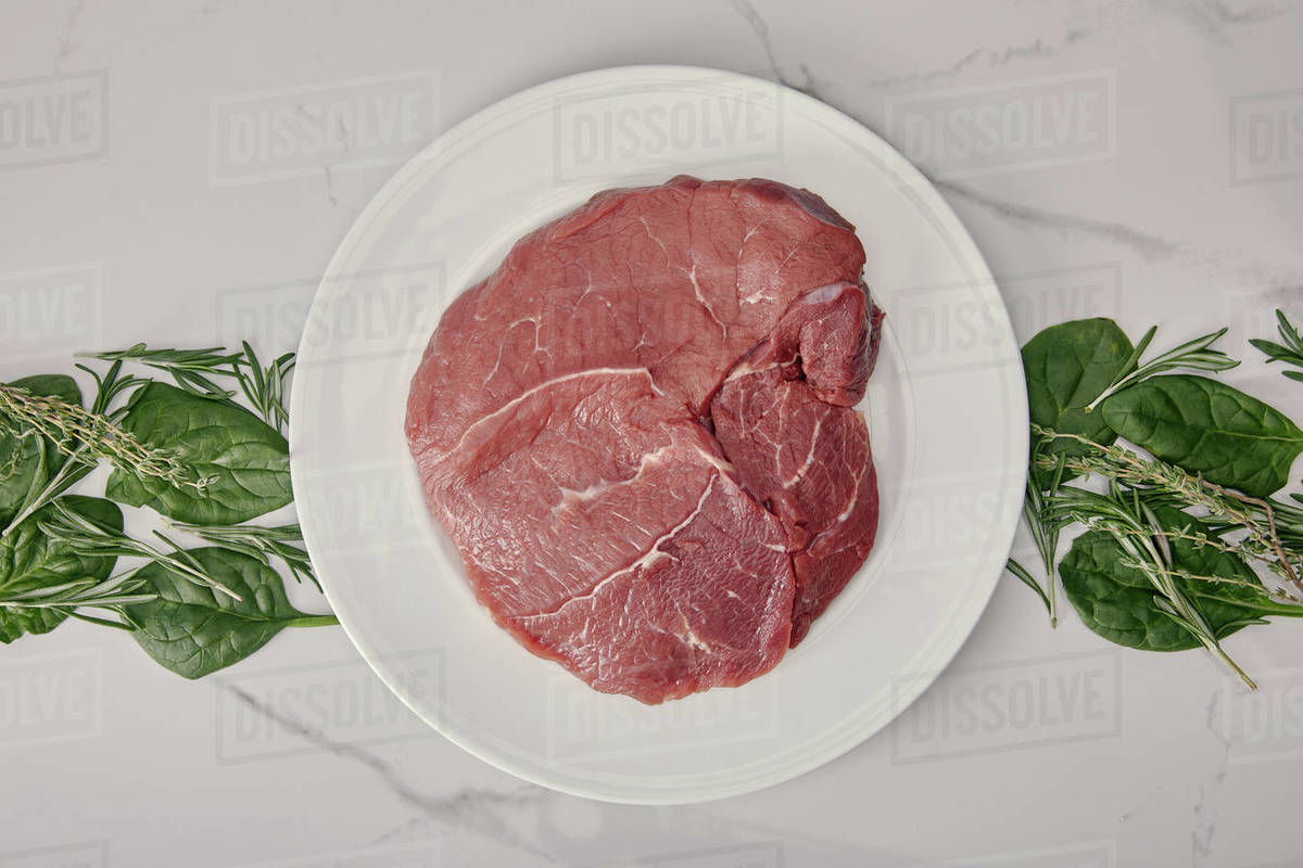 Top view of fresh raw meat on plate with herbs on white background ...