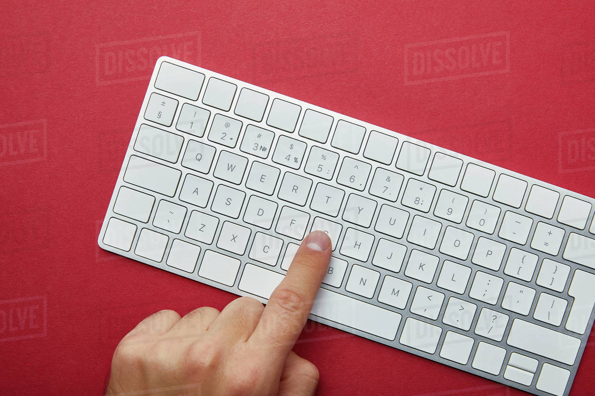 Cropped view of man pushing button on white computer keyboard on red ...