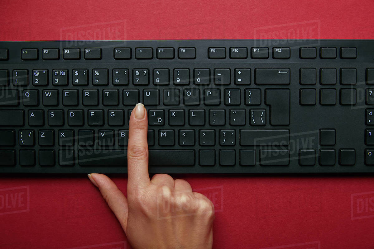 Cropped view of woman pushing button on black computer keyboard on red ...