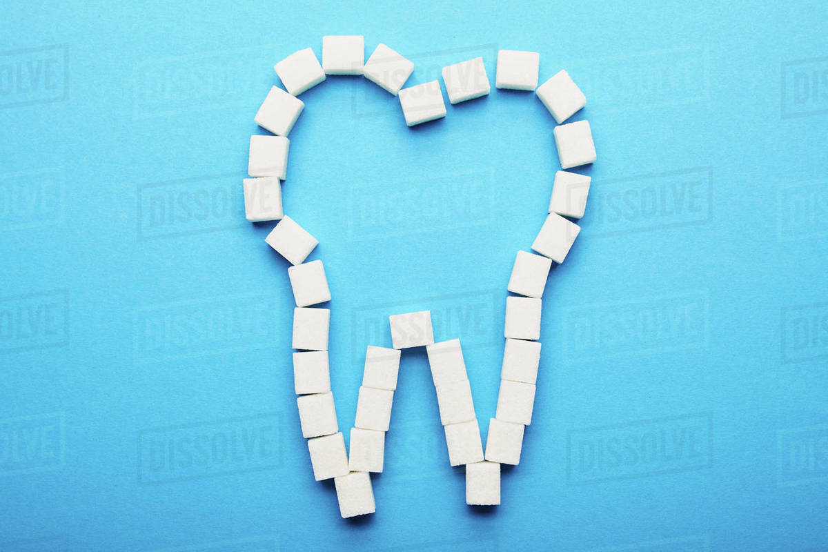 Top view of white sugar cubes arranged in tooth sign on blue background ...