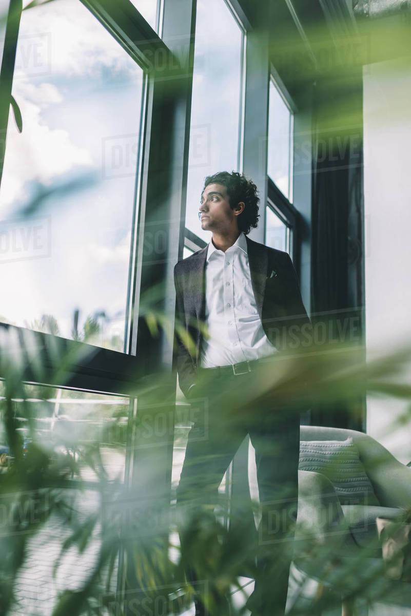 Pensive businessman looking out window while standing in office - Stock ...